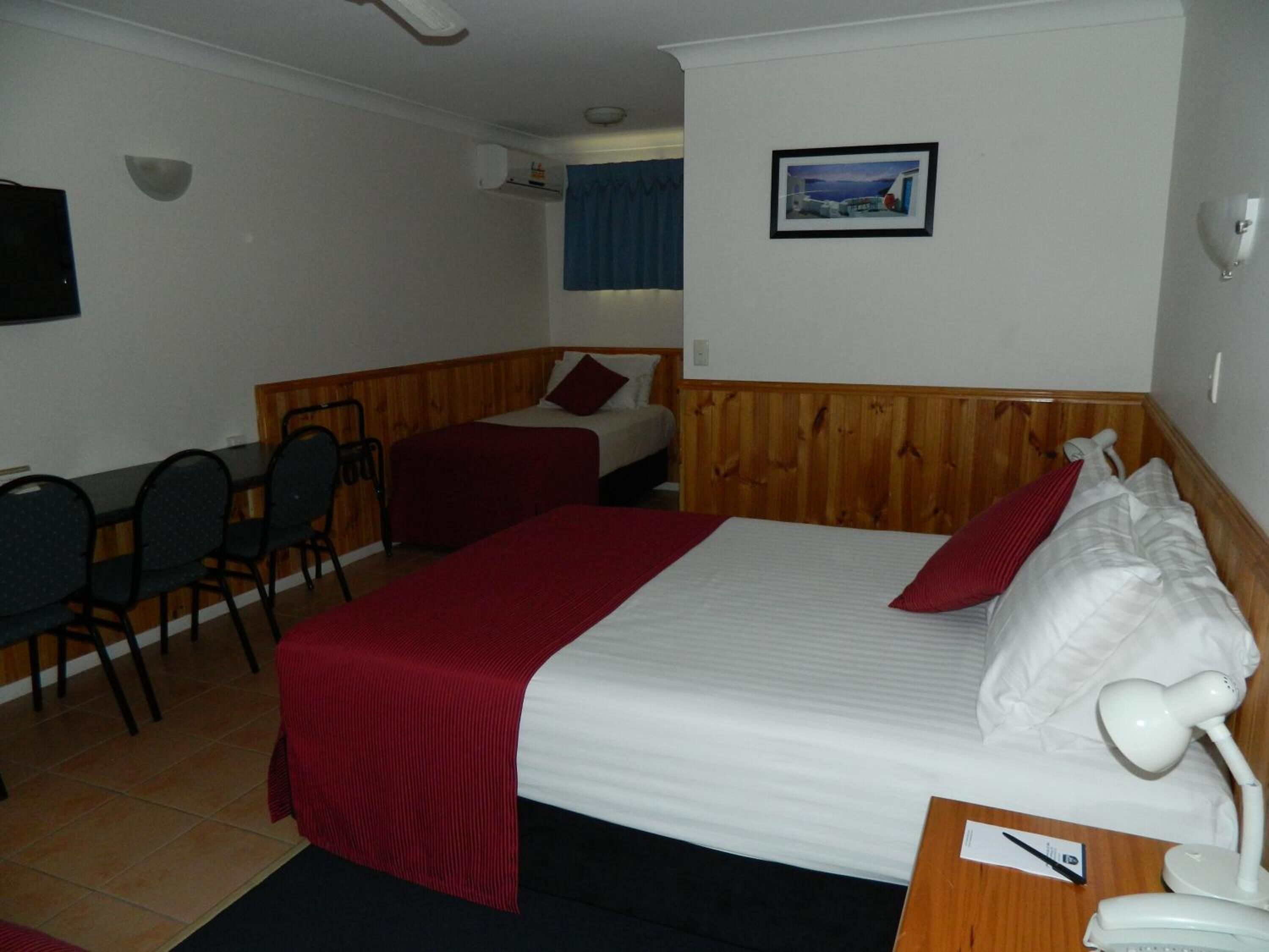 Quarto de hotel com cama, escrivaninha, cadeira e mesa pequena com abajur.
