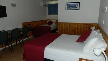 Quarto de hotel com cama, escrivaninha, cadeira e mesa pequena com abajur.