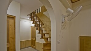 Uma escada de madeira com um ventilador branco fixado na parede, uma porta de madeira e um interruptor de luz na parede.