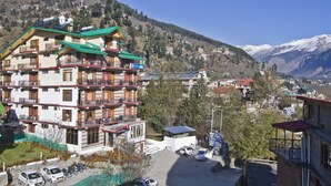 Um hotel com vários andares, varandas, área de estacionamento e vista para montanhas cobertas de neve.