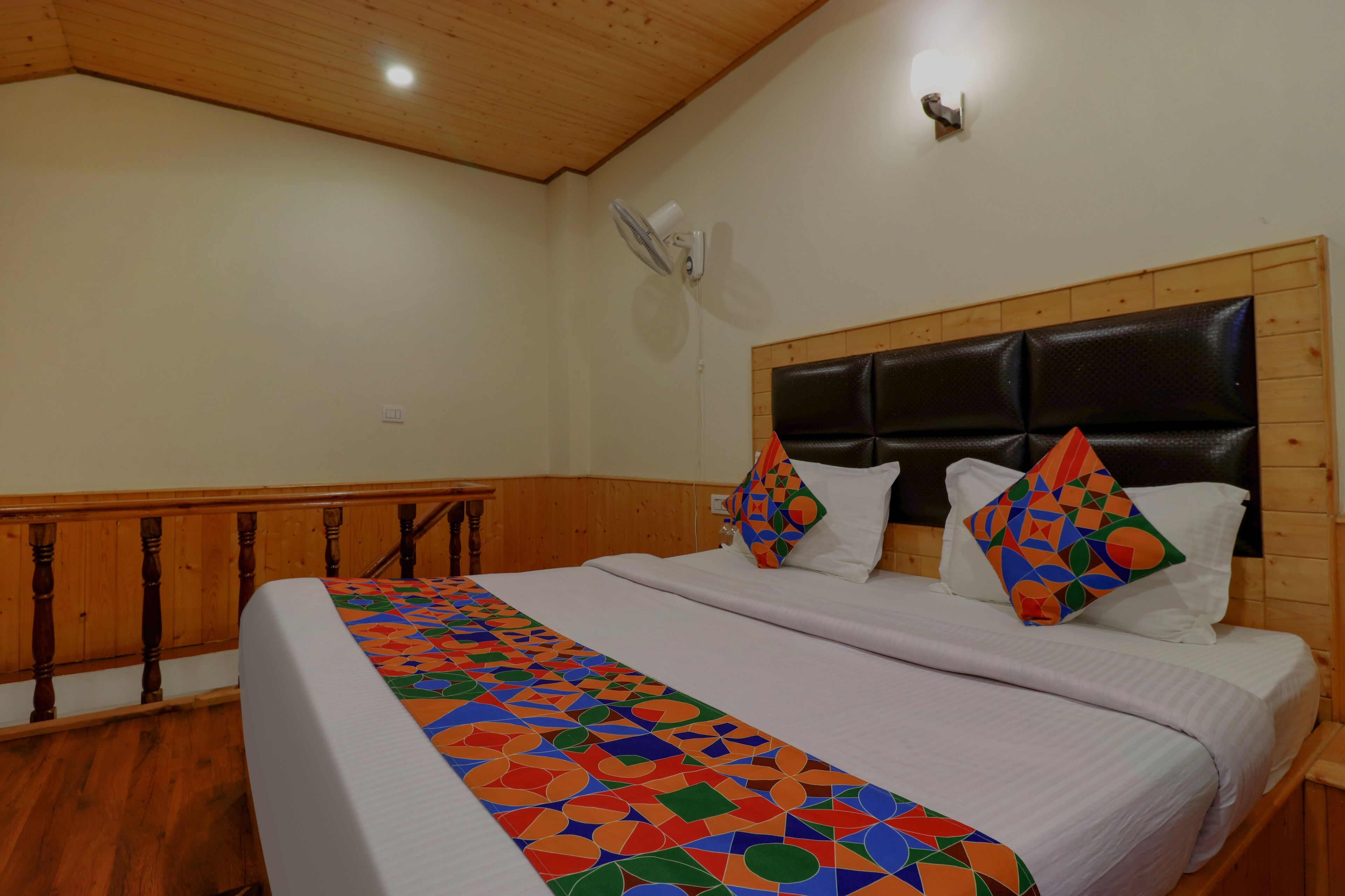 Quarto com cabeceira de madeira, cama com colcha de padrão geométrico colorido e ventilador de teto.