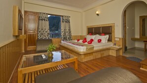 Um quarto de hotel acolhedor com chão de madeira, uma cama com balões vermelhos, uma mesa de centro de vidro, uma televisão e uma varanda com cortinas.