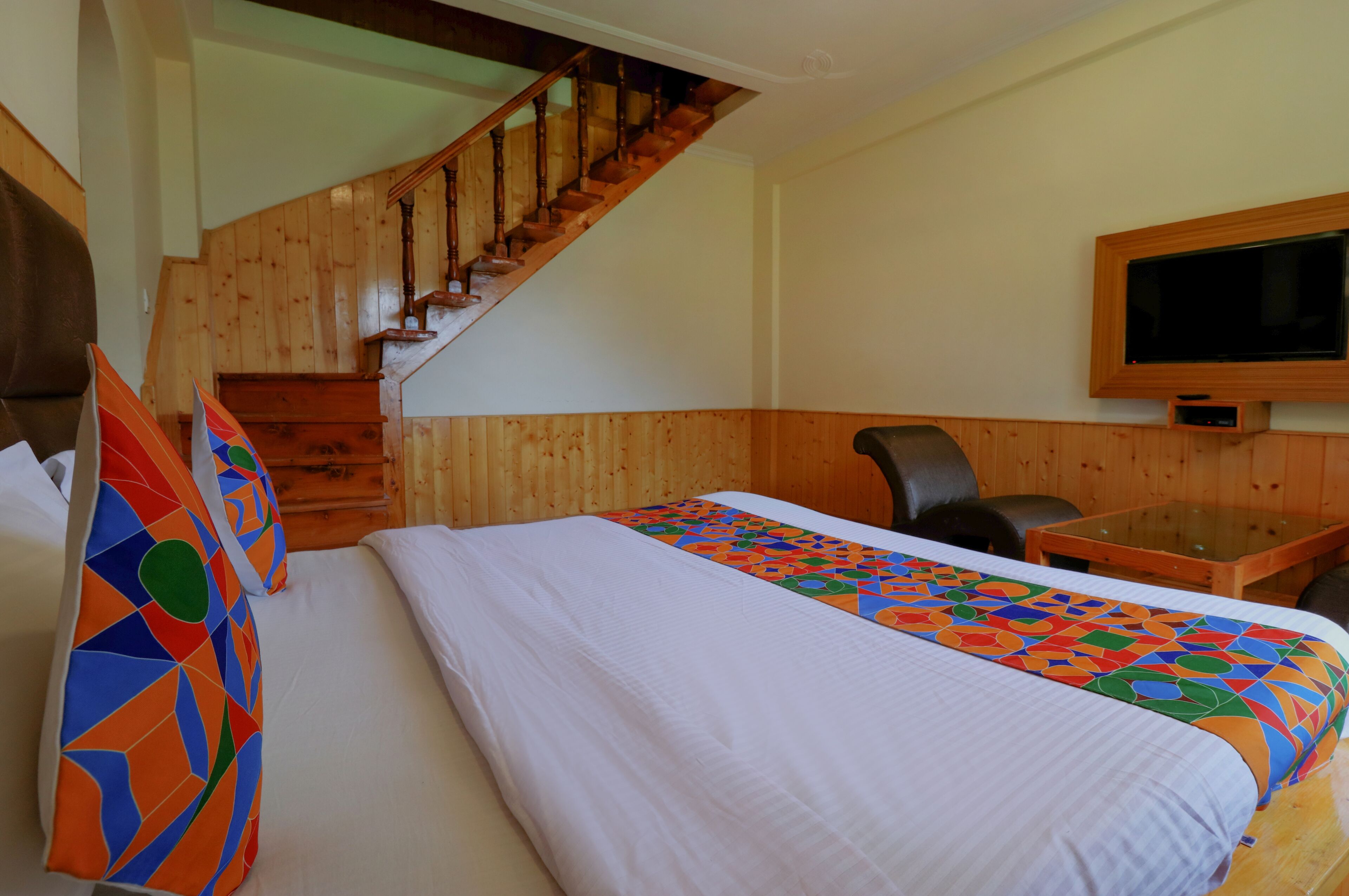 Quarto de hotel com uma cama, escada de madeira, televisão e uma mesinha.