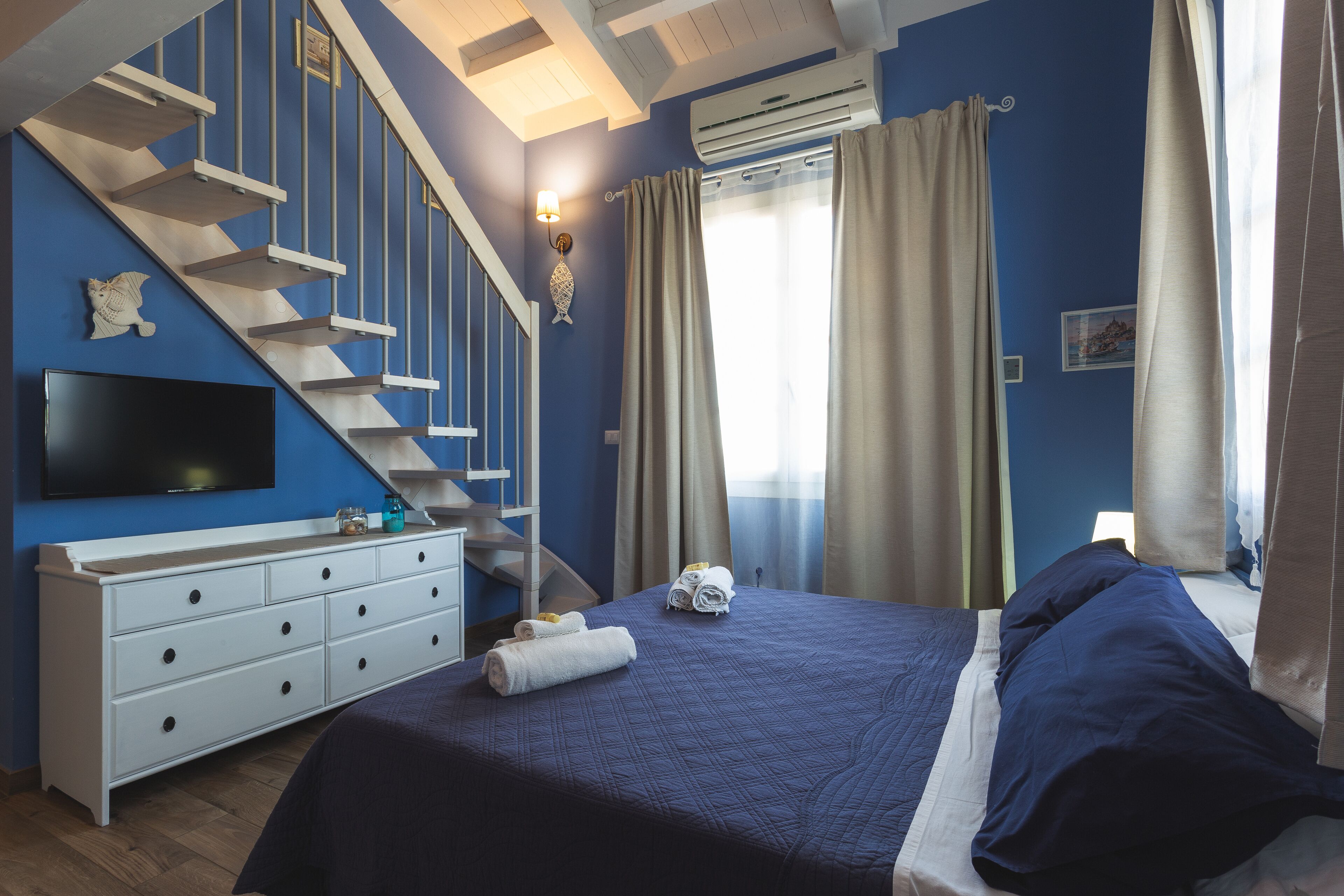 Quarto com cama, televisão, penteadeira, escada e ar condicionado.