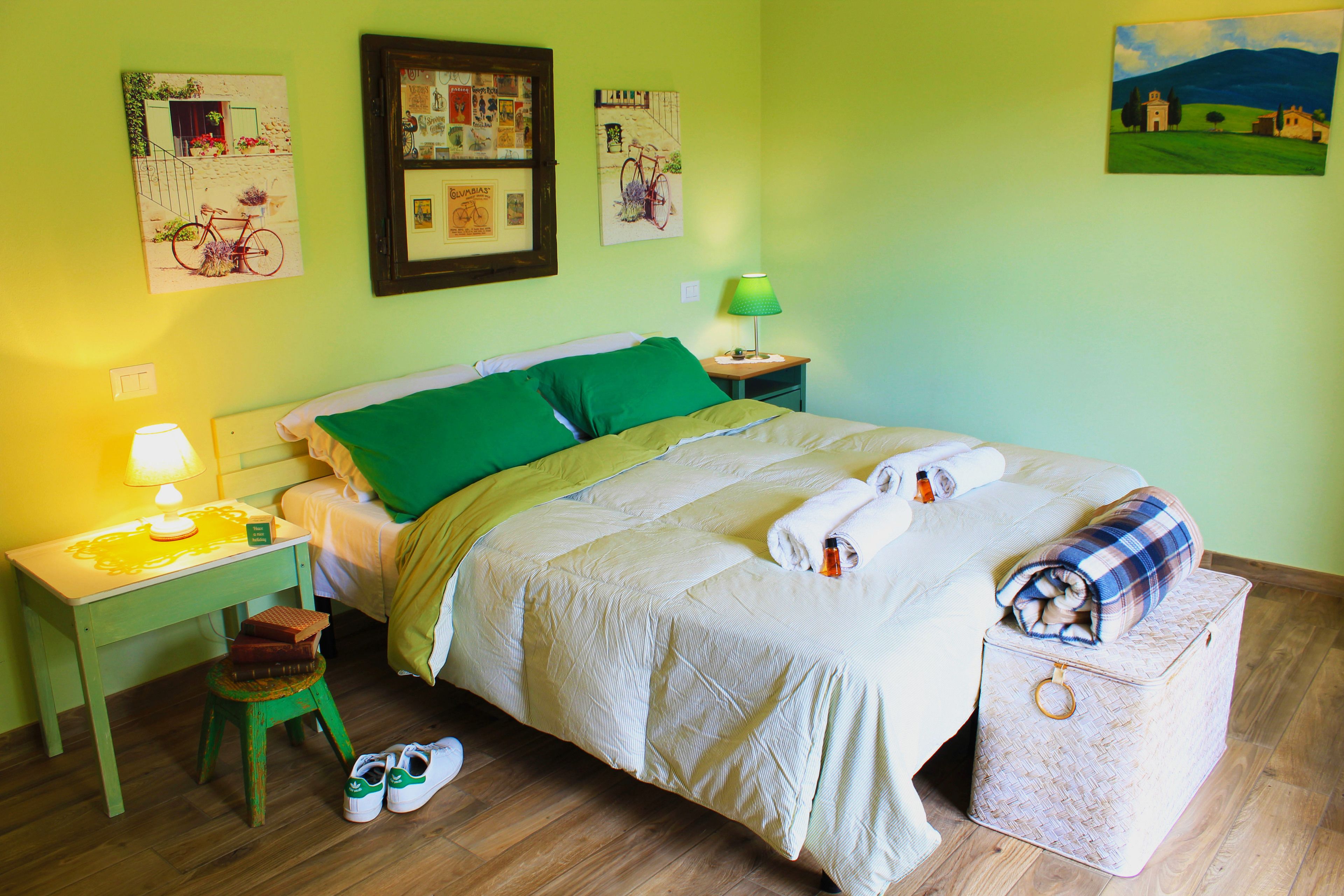 Quarto com cama, mesa de cabeceira, abajur, um banquinho e uma caixa organizadora.