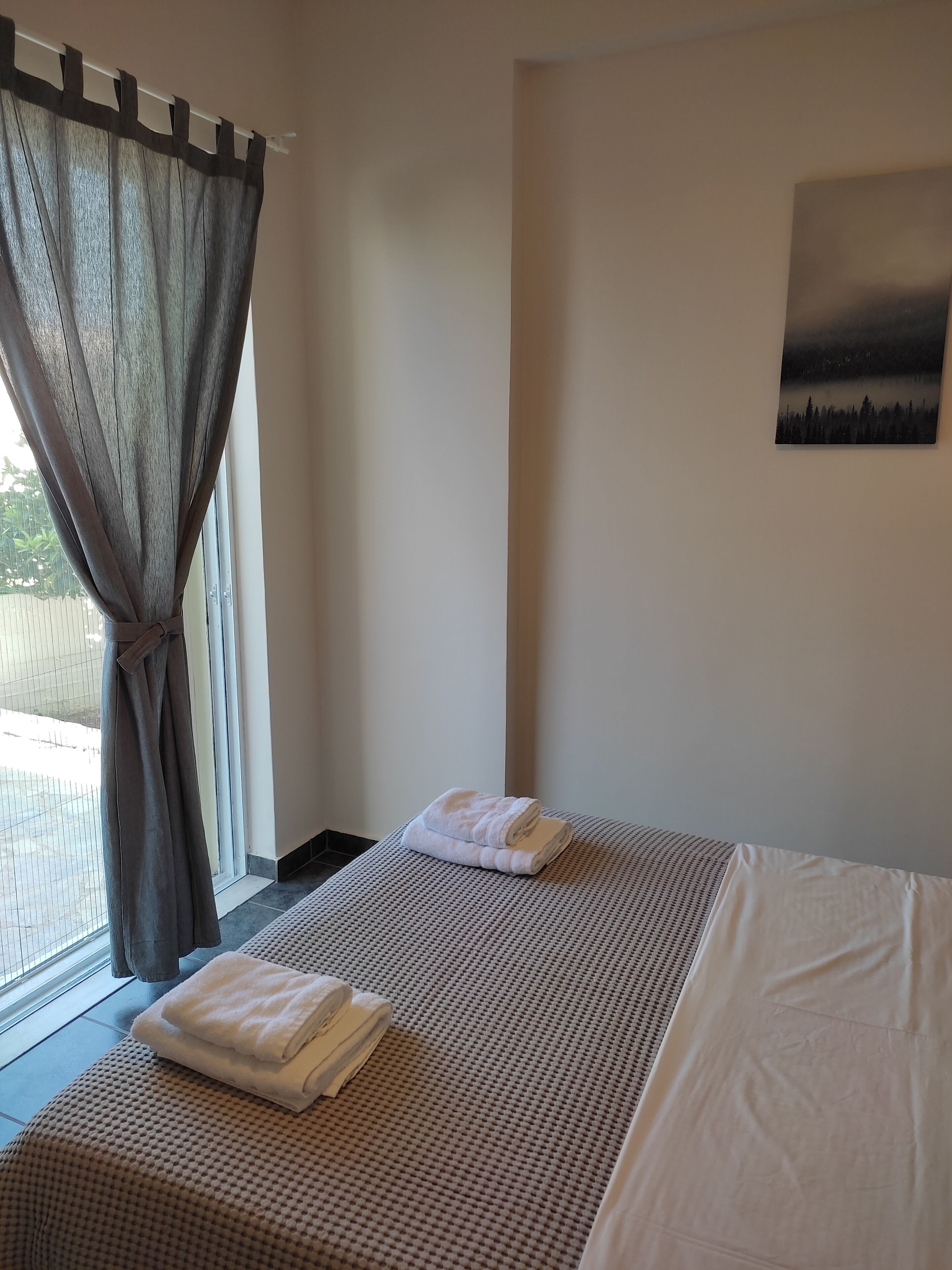 Quarto de hotel com cama, janela com cortinas, pintura na parede e vista para o exterior.