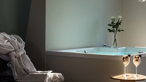 Casa de banho com banheira, uma toalha e dois copos com bebida sobre uma mesinha.