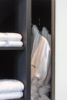 Quarto de hotel com armário contendo toalhas dobradas e um suporte com toalhas adicionais.