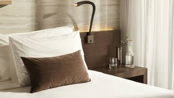 Quarto de hotel com cama, mesa de cabeceira, luminária na parede e janela com cortinas.