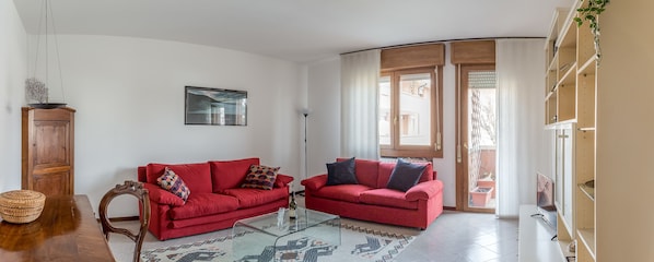 Uma sala de estar com dois sofás vermelhos, uma mesa de centro de vidro, um armário de madeira e uma janela grande com vista para o exterior.