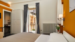 Quarto de hotel com cama, guarda-roupa, radiador, planta em vaso e vista para uma varanda externa.