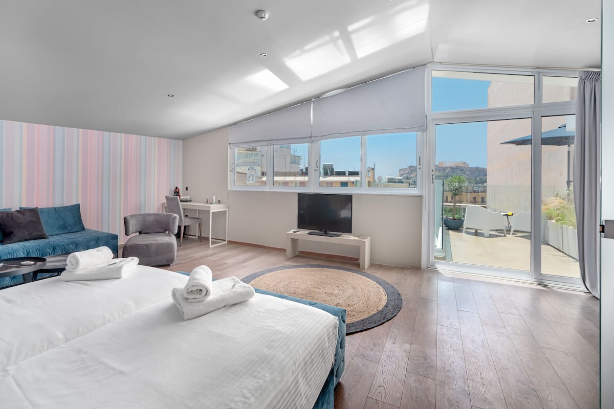 Quarto de hotel moderno com uma cama grande, uma mesa de escritório, televisão e varanda com vista para a cidade.