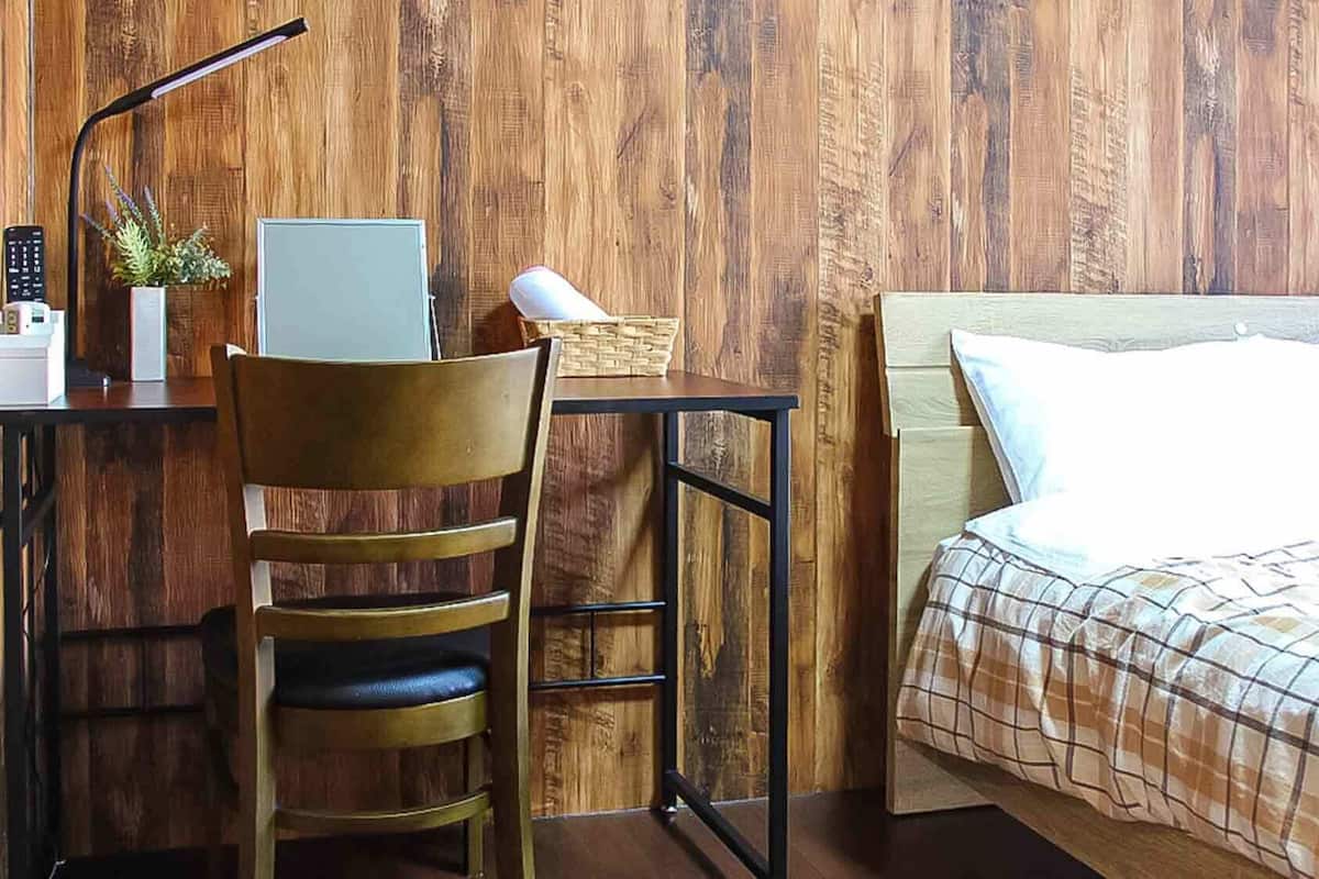 Um quarto de madeira com uma cama, uma escrivaninha, uma cadeira e um abajur.