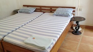 Quarto com duas camas, cada uma com roupa de cama e almofadas listradas. Há uma pequena mesa redonda com base decorativa ao lado das camas.