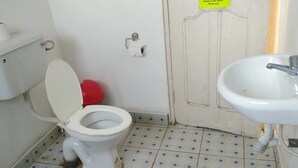 Uma casa de banho pequena com loiça sanitária branca, assento vermelho, lavatório branco e suporte para papel higiénico.