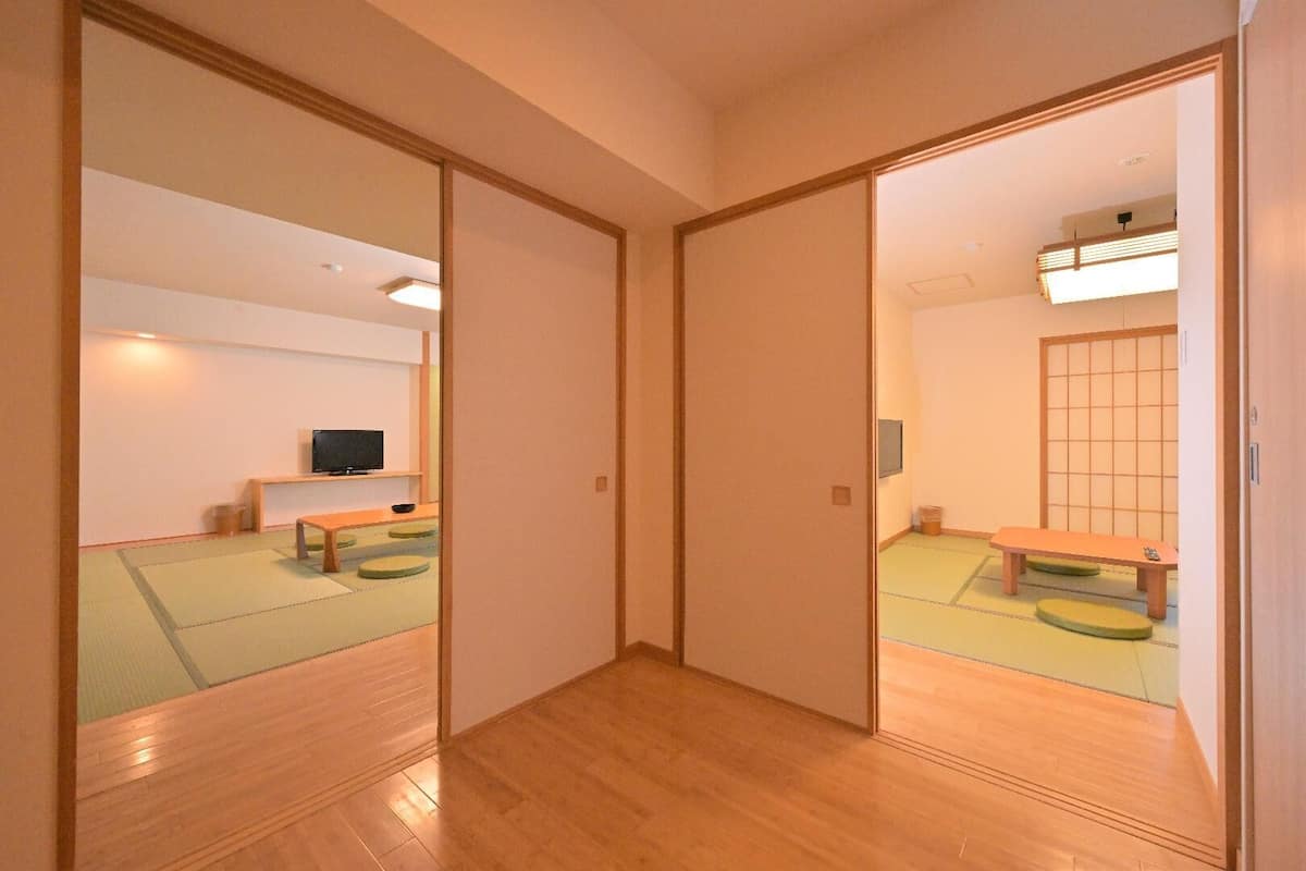 Quarto japonês tradicional com tatames, uma mesa de madeira baixa, uma televisão e uma porta deslizante.