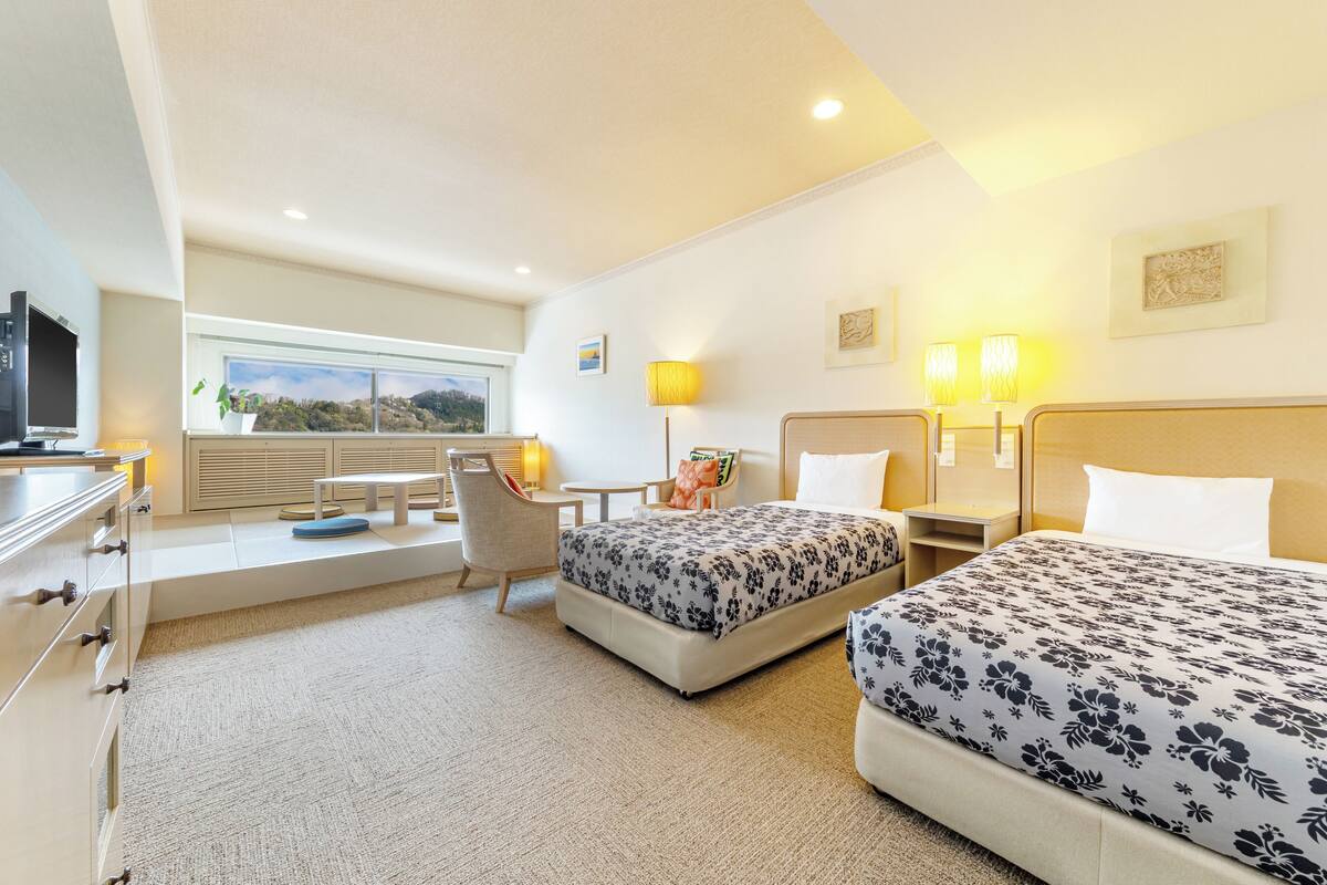 Quarto de hotel com duas camas, uma escrivaninha, uma cadeira, uma televisão e janela com vista.