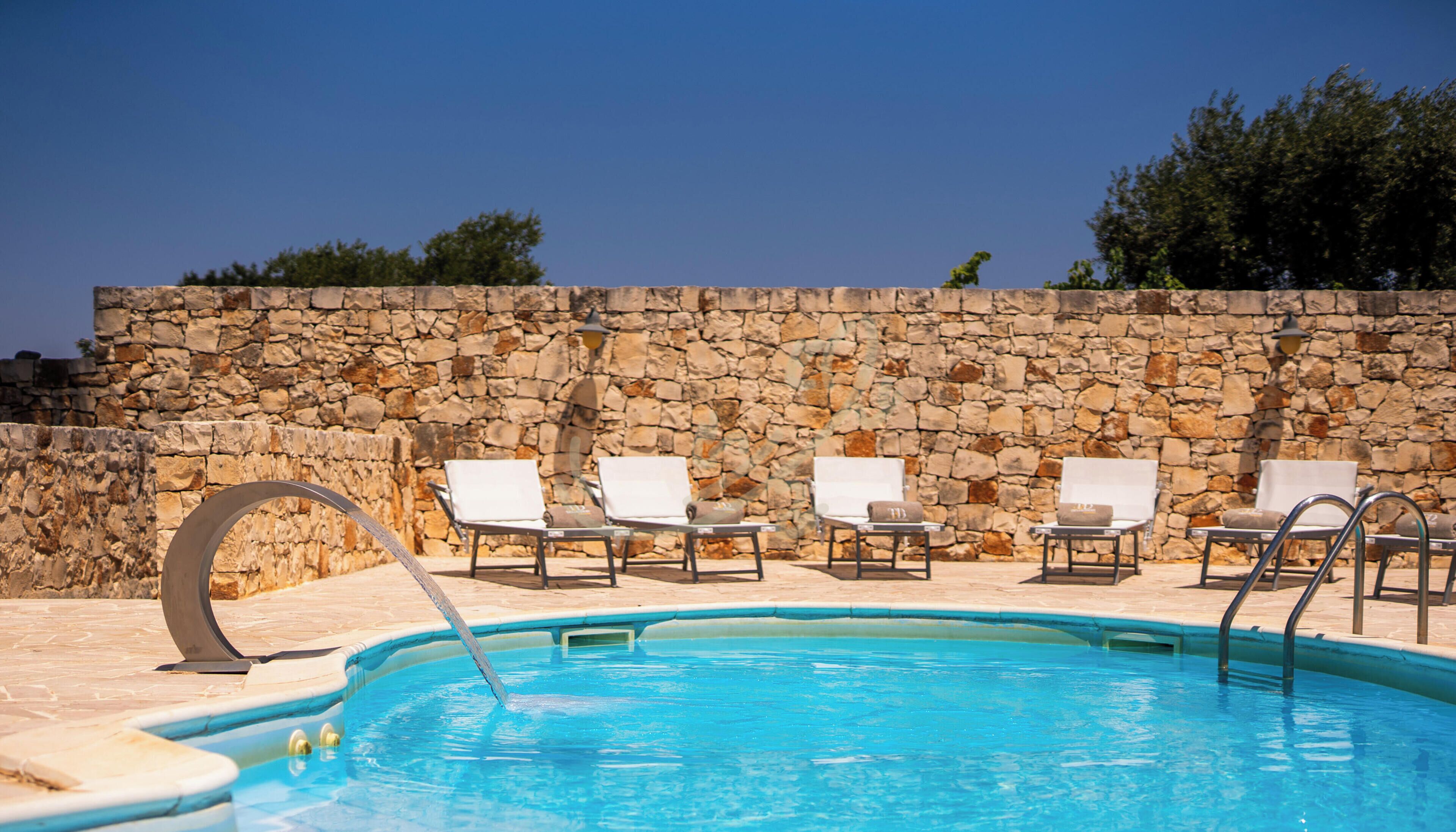Piscina com espreguiçadeiras e muro de pedra.