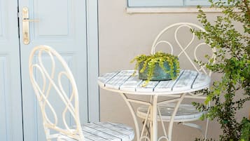 Conjunto de mesa e cadeira de metal branco sobre um deck de madeira, com um vaso de planta ao lado.
