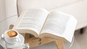 Um livro aberto sobre uma mesa de vidro, com uma xícara de café ao lado.