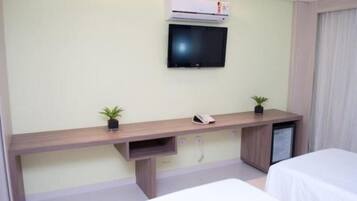 Quarto de hotel com cama, escrivaninha com telefone, uma planta pequena e ar condicionado.