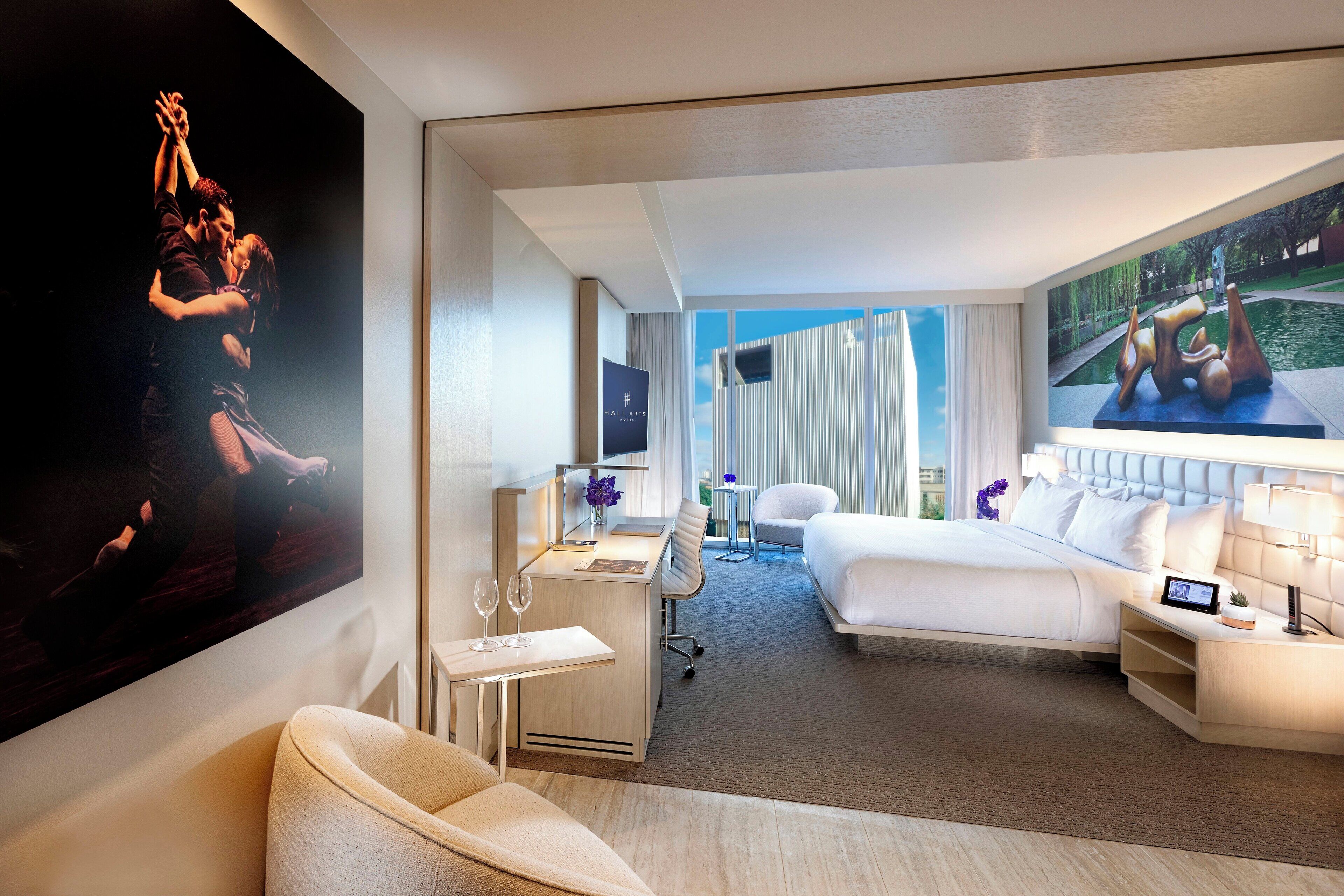 Quarto de hotel com cama, escrivaninha, cadeira, televisão e uma grande pintura na parede.
