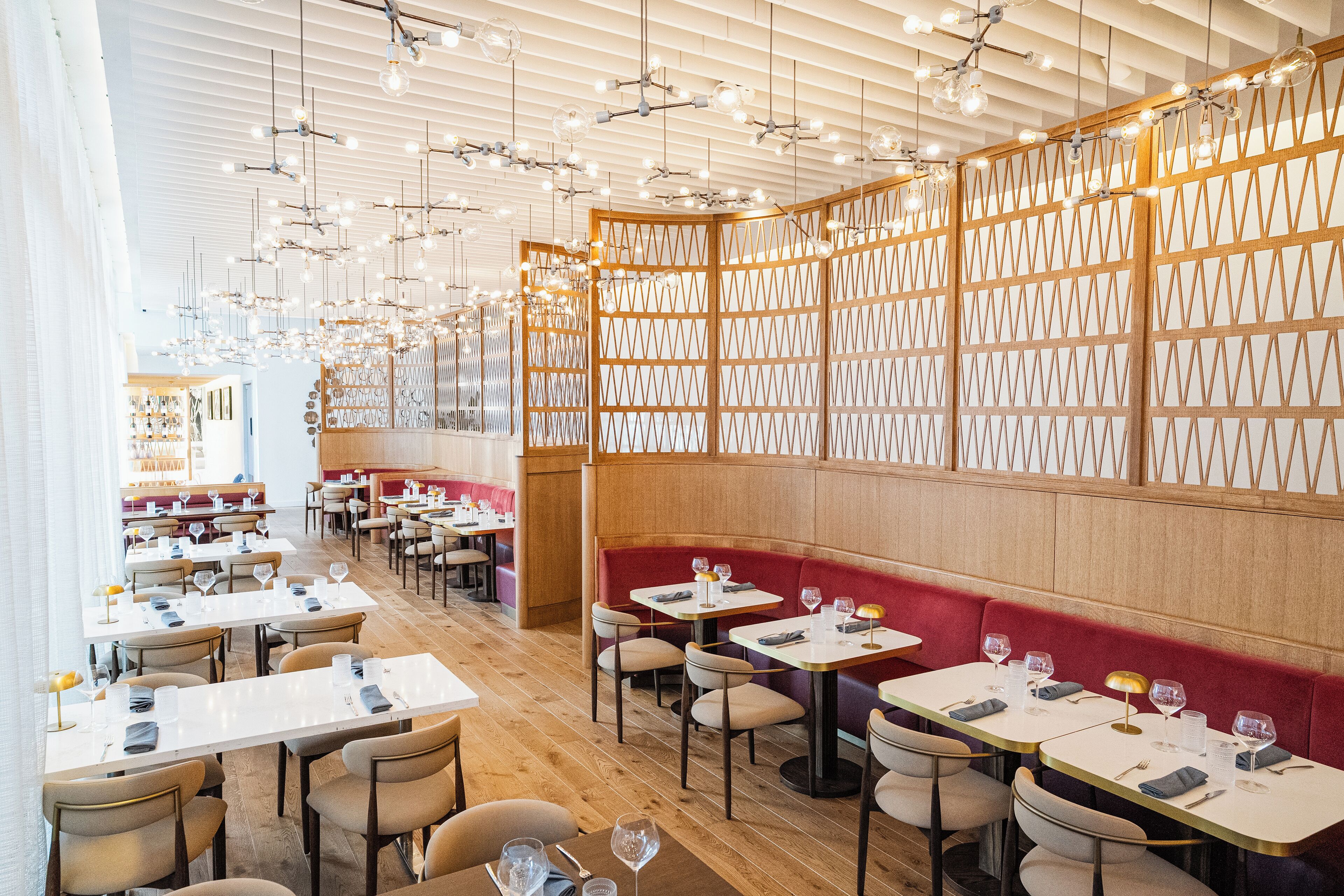 Interior moderno de restaurante com divisórias de madeira, mesas brancas e luminárias pendentes.