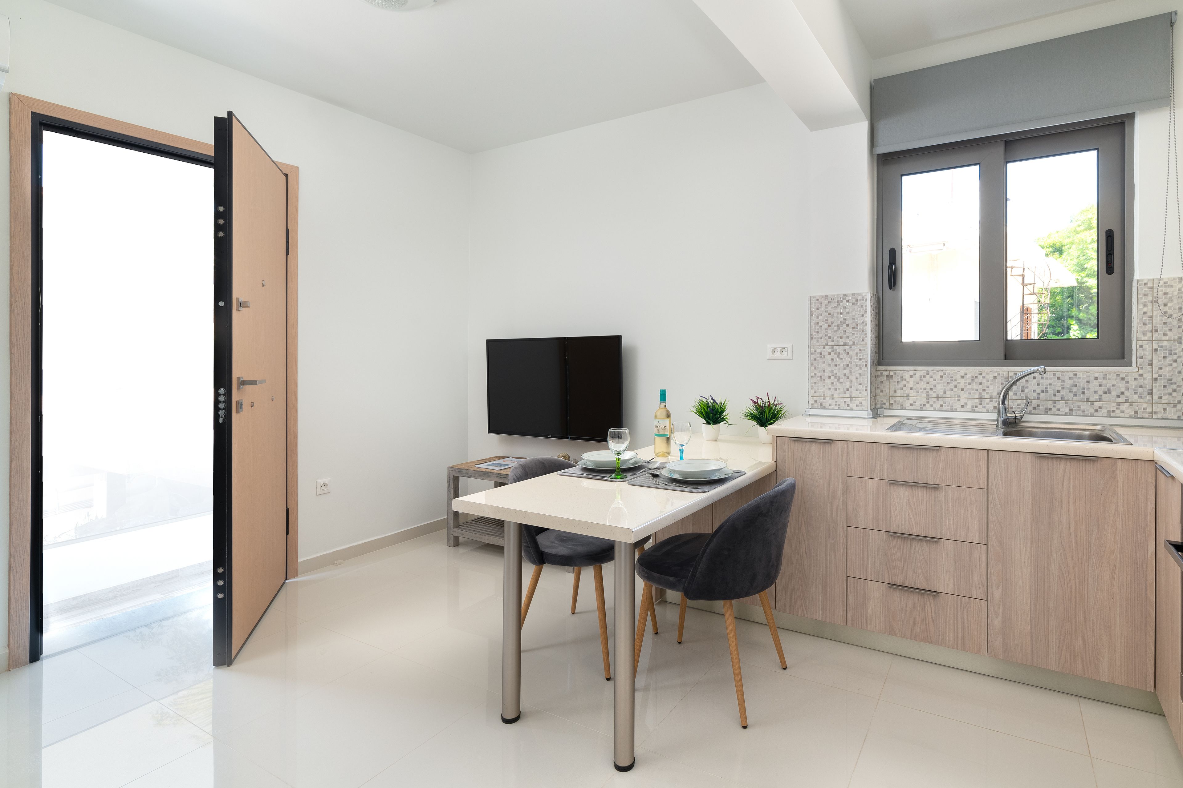 Cozinha moderna com mesa de jantar, cadeiras, televisão e janela.