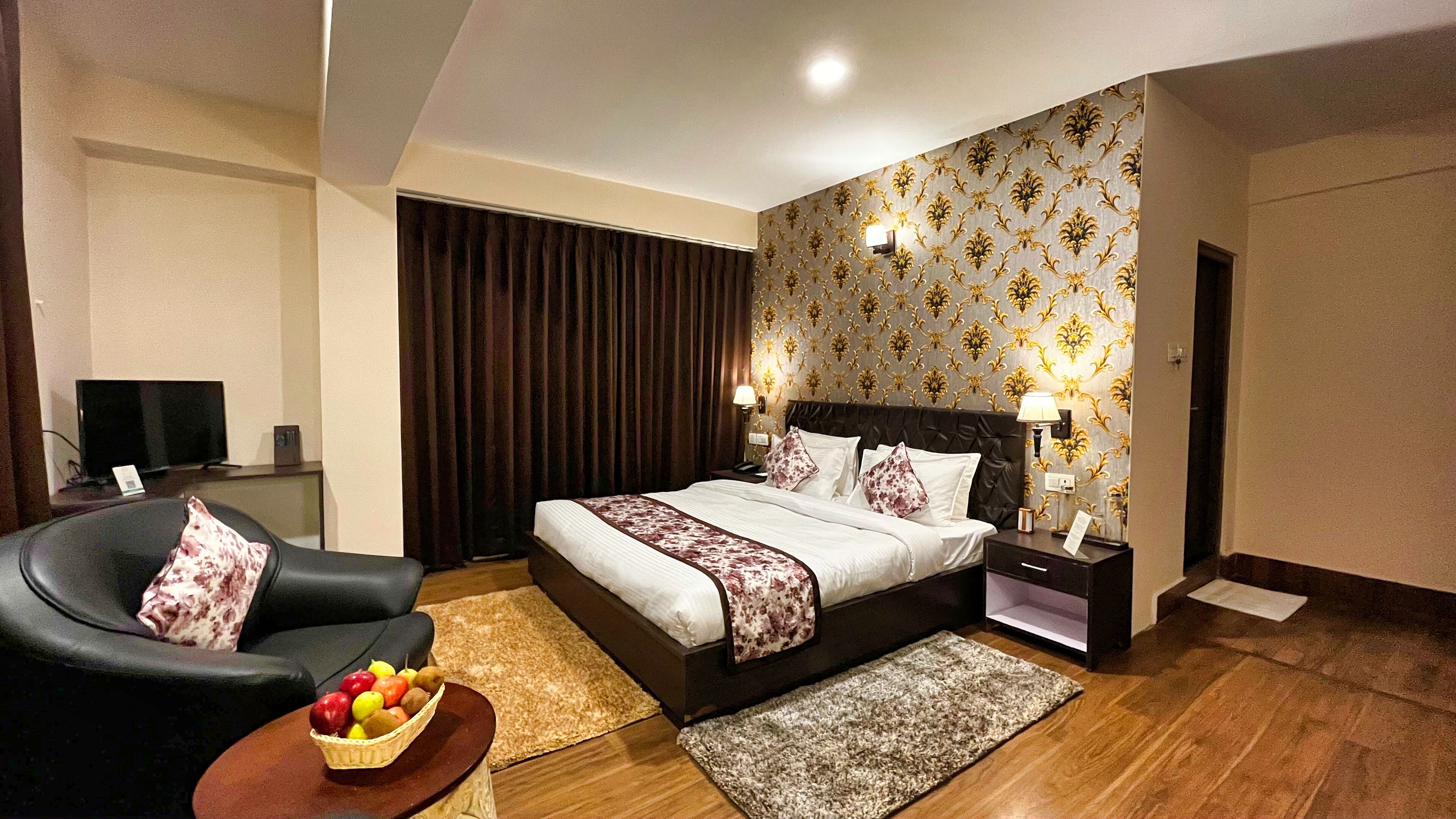 Quarto de hotel com cama, uma cadeira, uma mesinha com frutas e televisão.