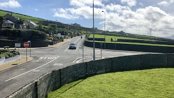 Uma estrada com uma placa de pare, um carro e uma área gramada com um muro de pedra.
