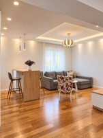 Uma sala de estar moderna com um sofá, uma poltrona floral, uma mesinha e uma escrivaninha de madeira com uma cadeira.