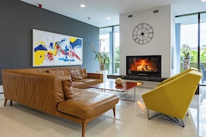 Uma sala de estar moderna com um sofá de couro, uma poltrona amarela, uma lareira e arte abstrata na parede.