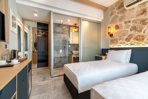 Quarto de hotel com cama, mesa de cabeceira e banheiro com chuveiro e pia.
