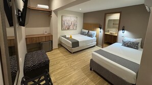 Quarto de hotel moderno com duas camas, uma secretária pequena, um espelho e um banheiro visível por uma porta aberta.