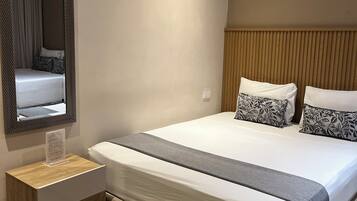 Quarto de hotel com uma cama grande, uma mesa de cabeceira, um espelho e um painel de cabeceira de madeira.
