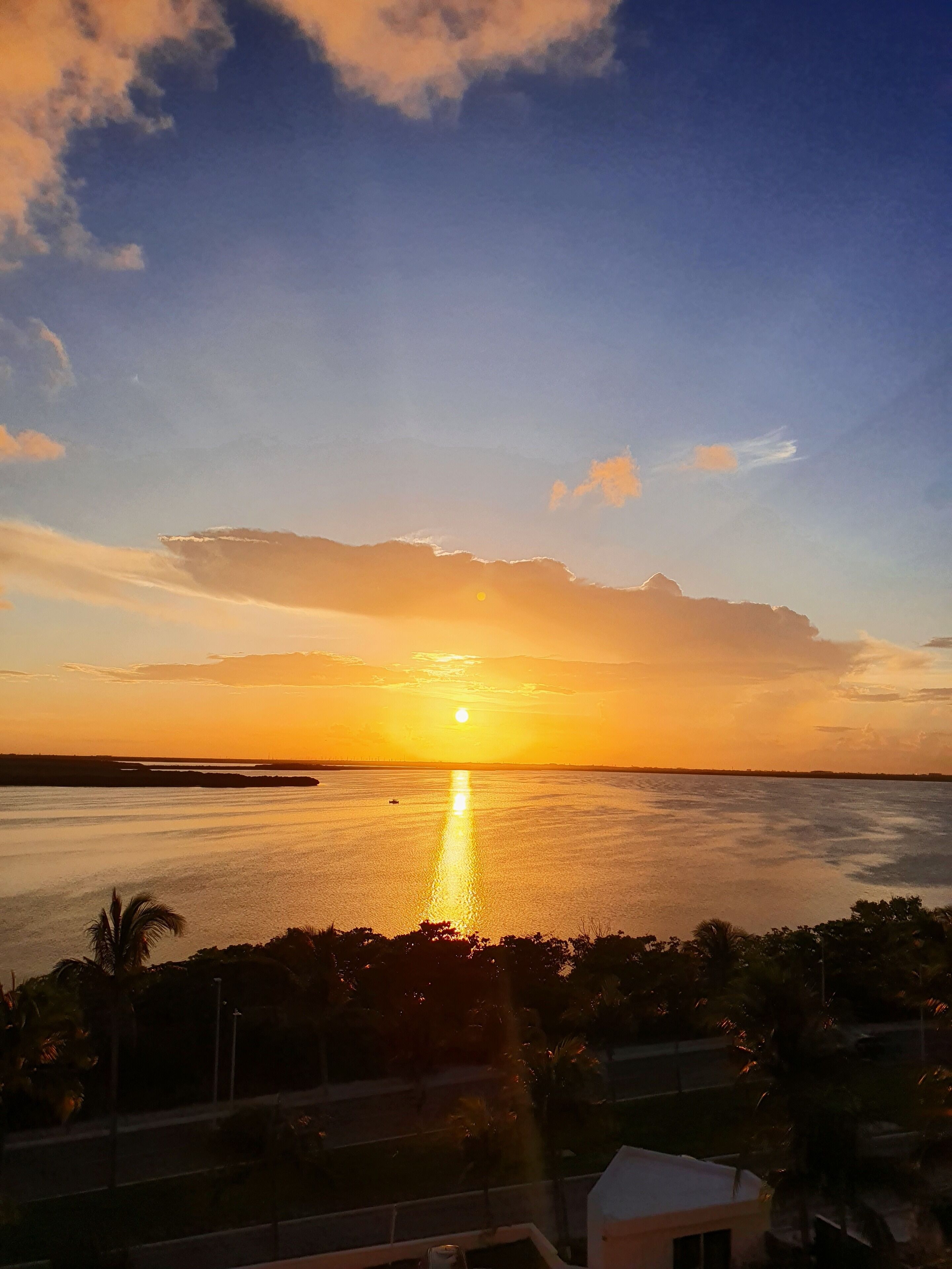 Pôr do sol sobre águas calmas, com uma linha de costa distante.