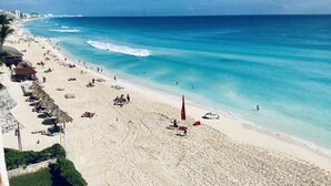 Uma praia com águas turquesa cristalinas, areal arenoso e alguns guarda-sóis e cadeiras de praia.