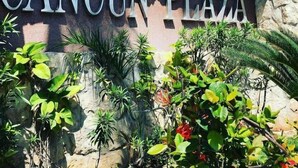 Placa para o Cancun Plaza, com uma parede de pedra e diversas plantas na frente.