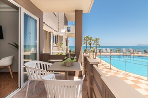 Uma varanda com piscina, cadeiras brancas e uma mesa com uma cesta de uvas.