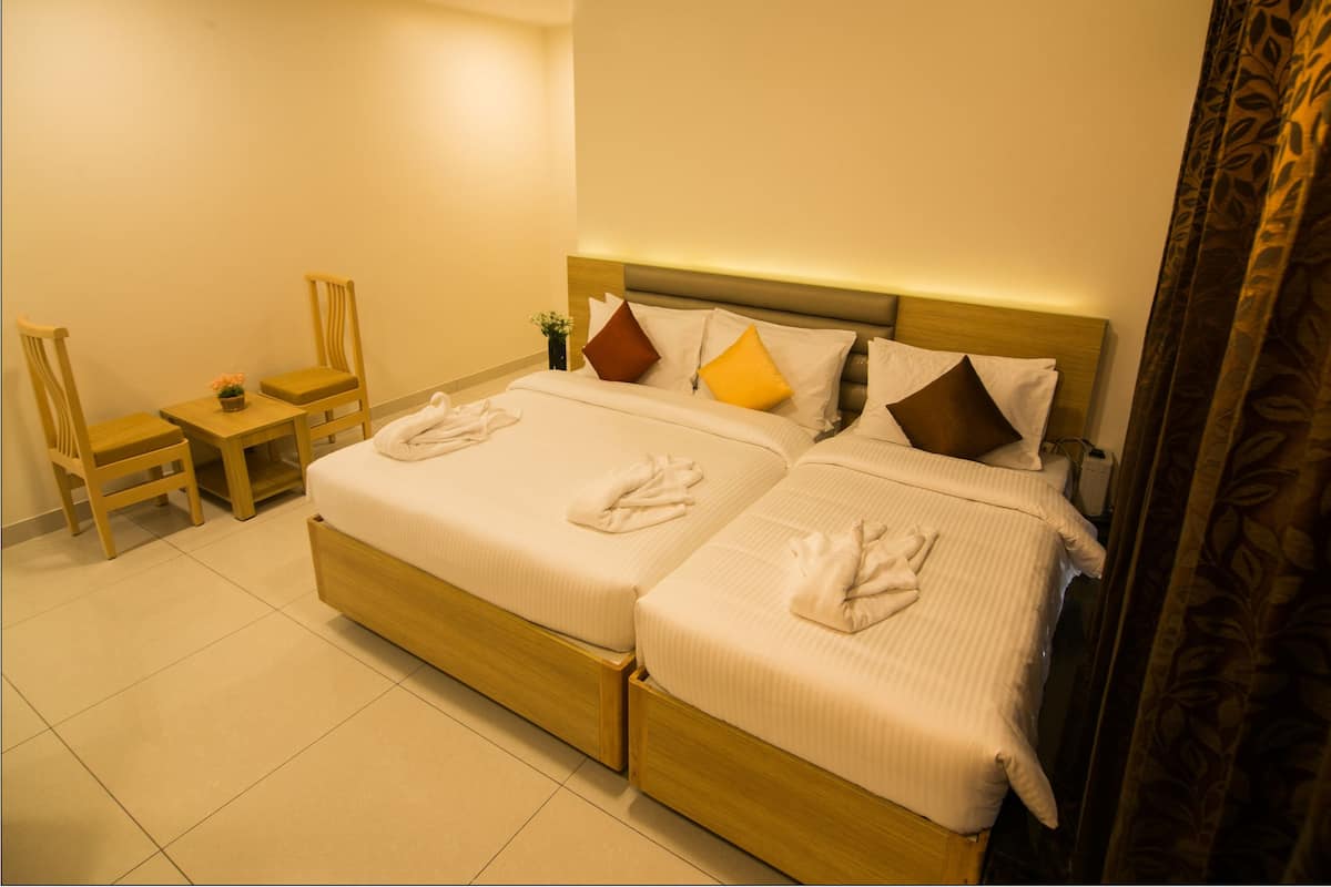 Cama de casal com duas almofadas, uma mesinha de cabeceira e uma cadeira num quarto de hotel.