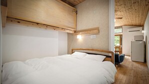 Quarto com teto de madeira, cama com roupa de cama branca, cabeceira de madeira, luminária na parede e aparelho de ar condicionado.