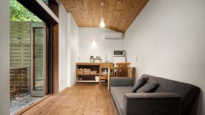 Um quarto pequeno com piso de madeira, um sofá cinza, uma mesa de madeira e uma porta de vidro deslizante que dá para o exterior.