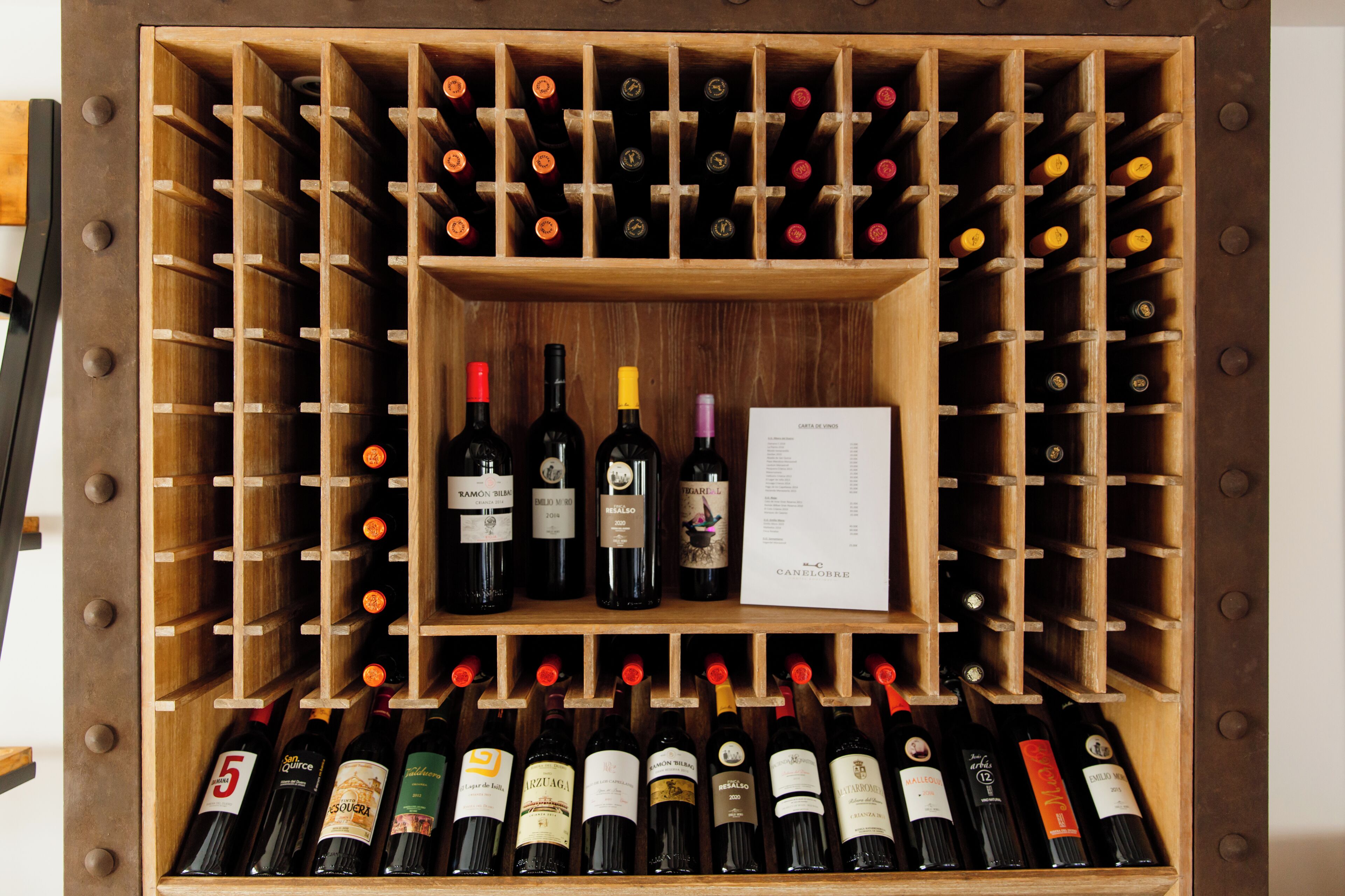 Estante de madeira com várias garrafas de vinho e um cartão de menu.
