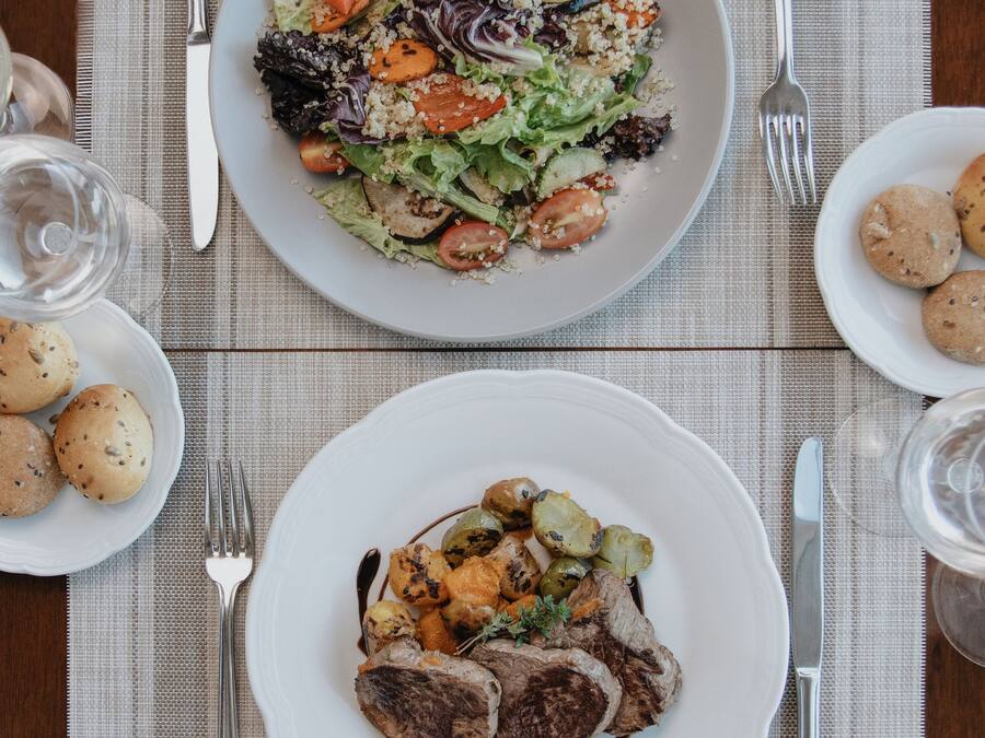 Uma mesa de jantar com dois pratos de comida, um garfo, uma faca e um copo de água.