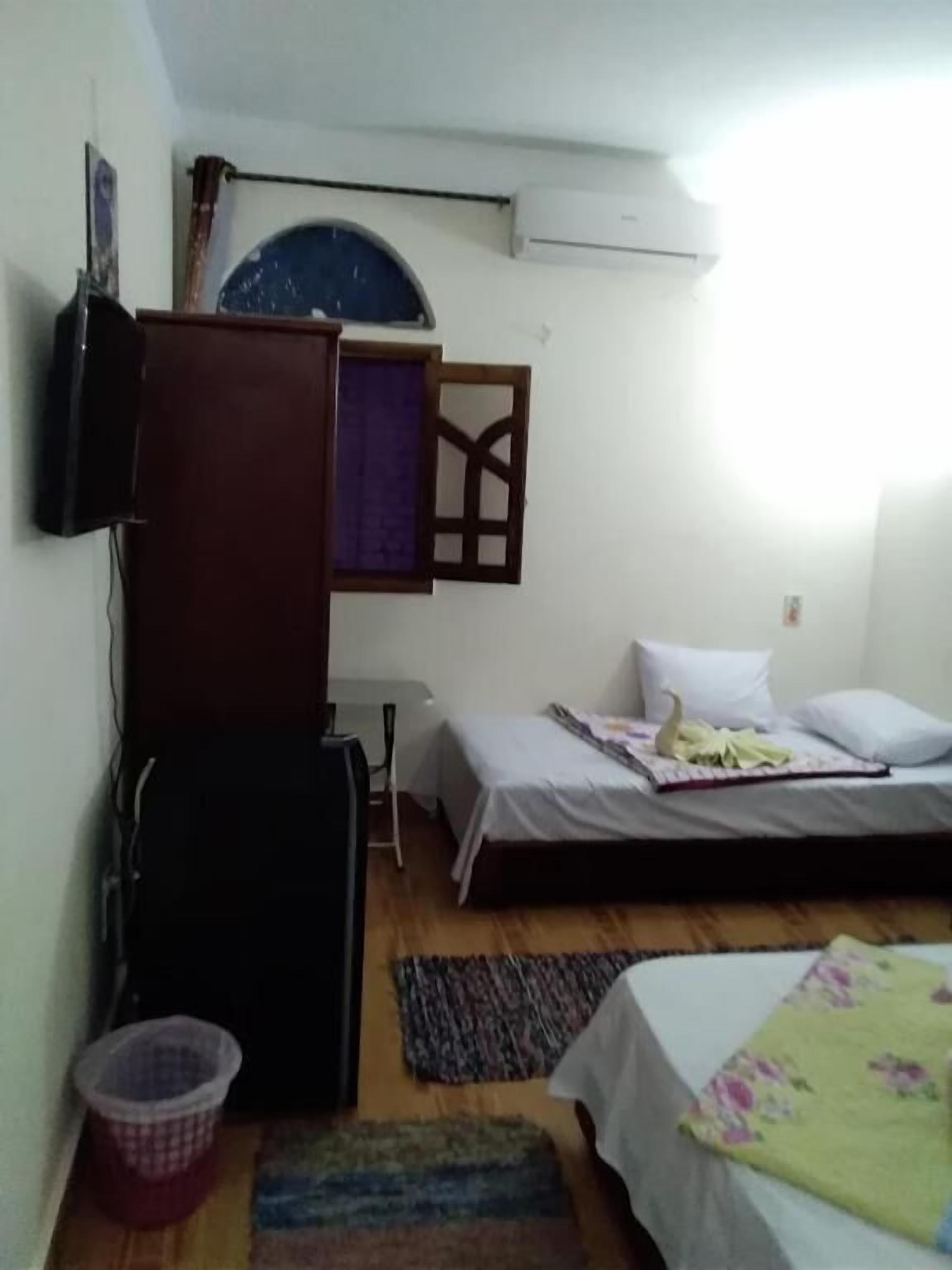 Um quarto pequeno e simples com uma cama, uma escrivaninha, um guarda-roupa e uma televisão.