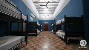 Quarto de hostel com beliches, piso xadrez e ventilador de teto.