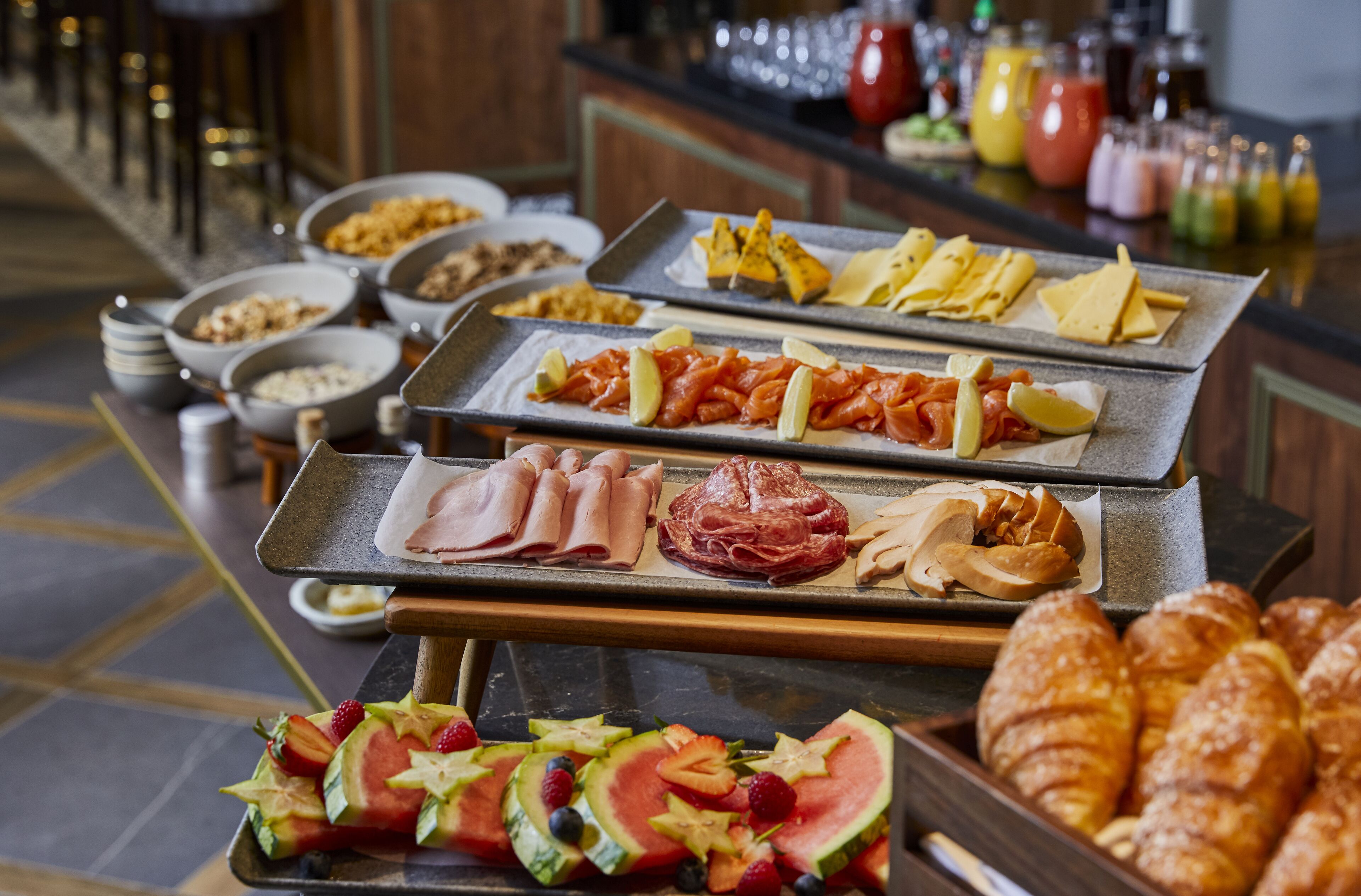 Buffet com diversos itens de comida, incluindo carnes, queijos, frutas e doces.