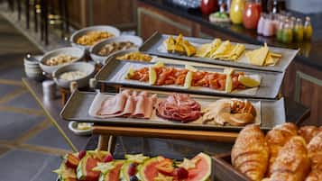 Buffet com diversos itens de comida, incluindo carnes, queijos, frutas e doces.