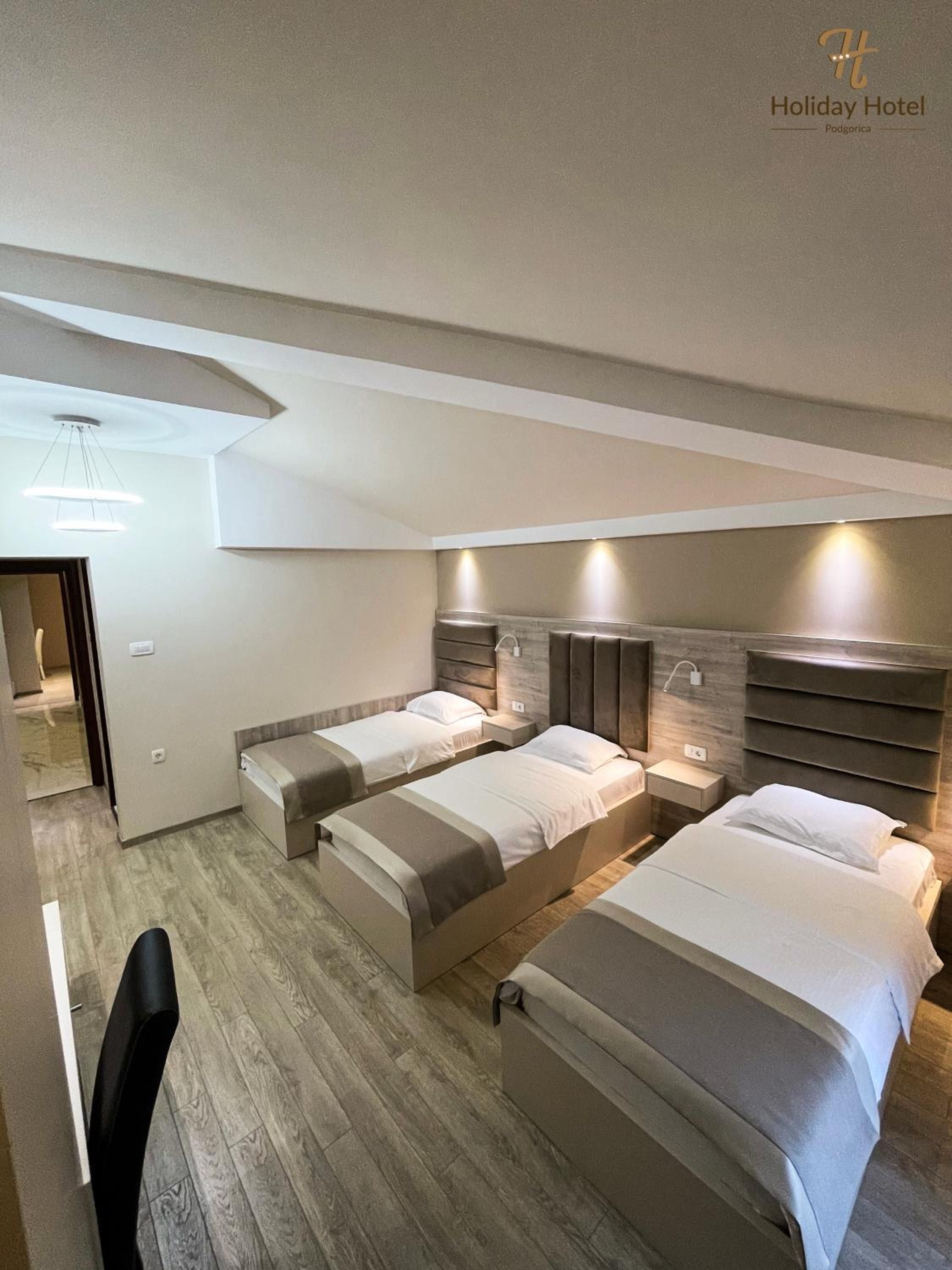 Quarto moderno com três camas, piso de madeira e luminária no teto.