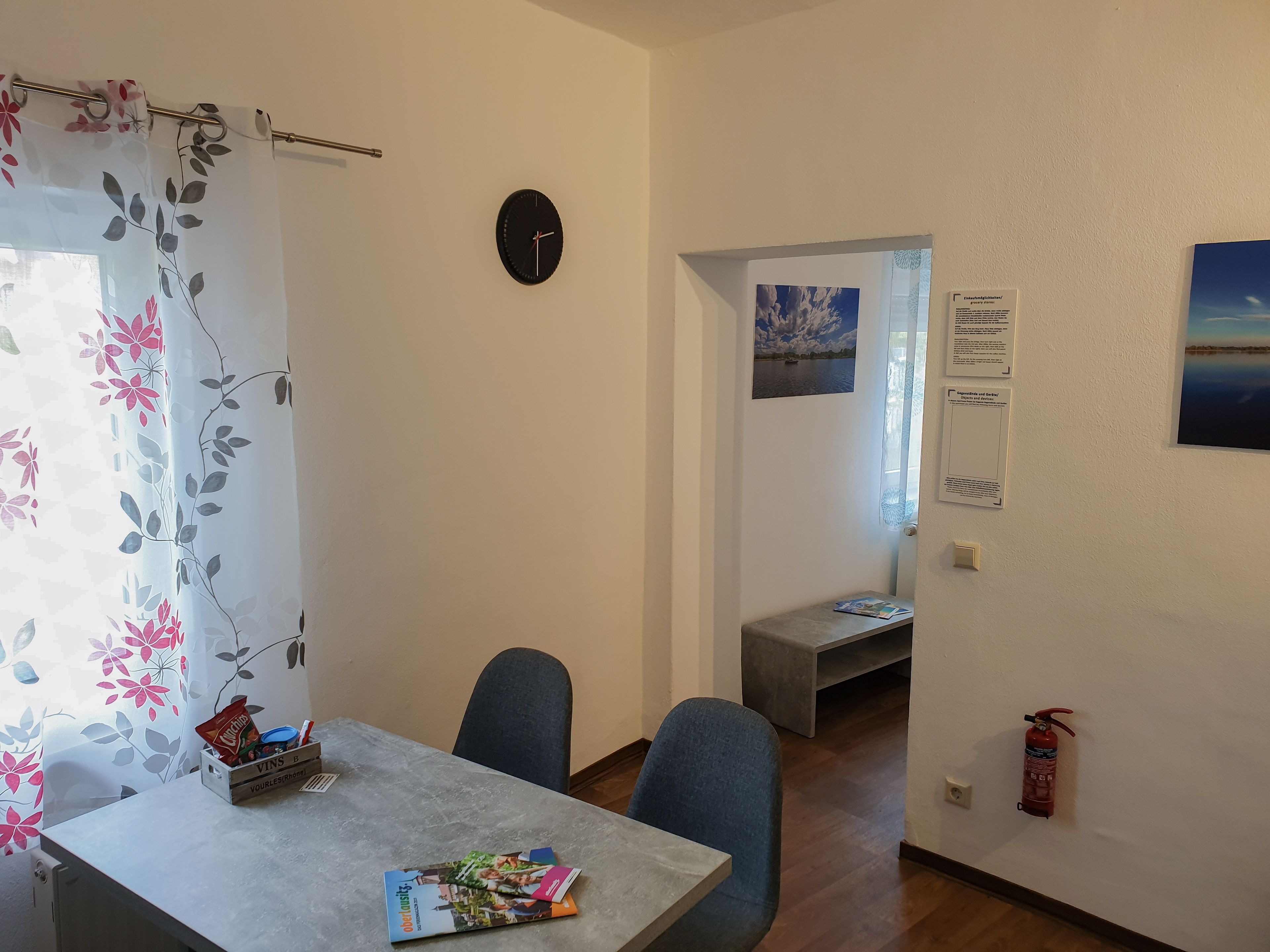 Quarto moderno com uma mesa de jantar, cadeiras, um relógio, um extintor de incêndio e vista para um lago pela janela.